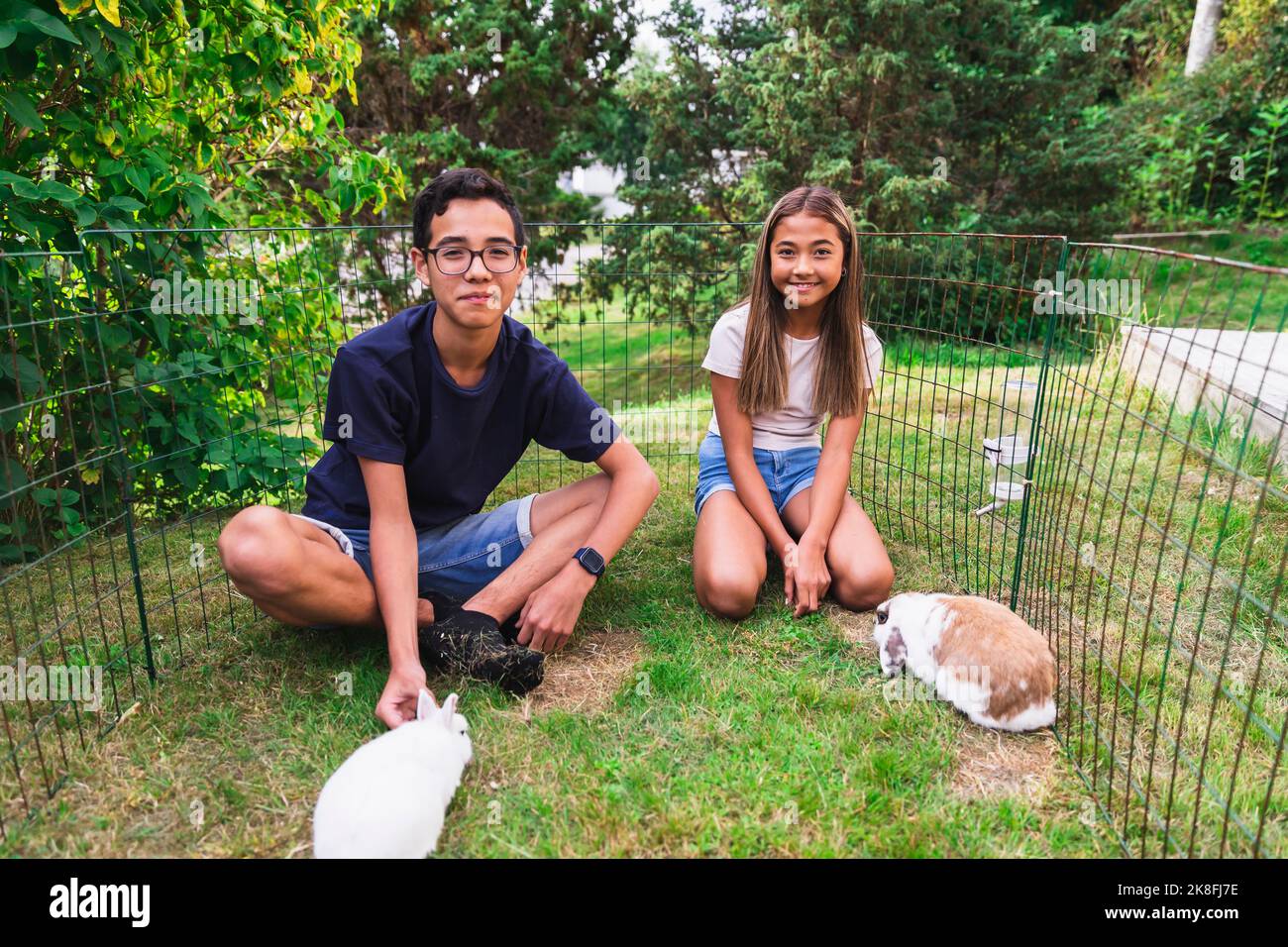Brother and sister spending leisure time with rabbits amidst fence in ...