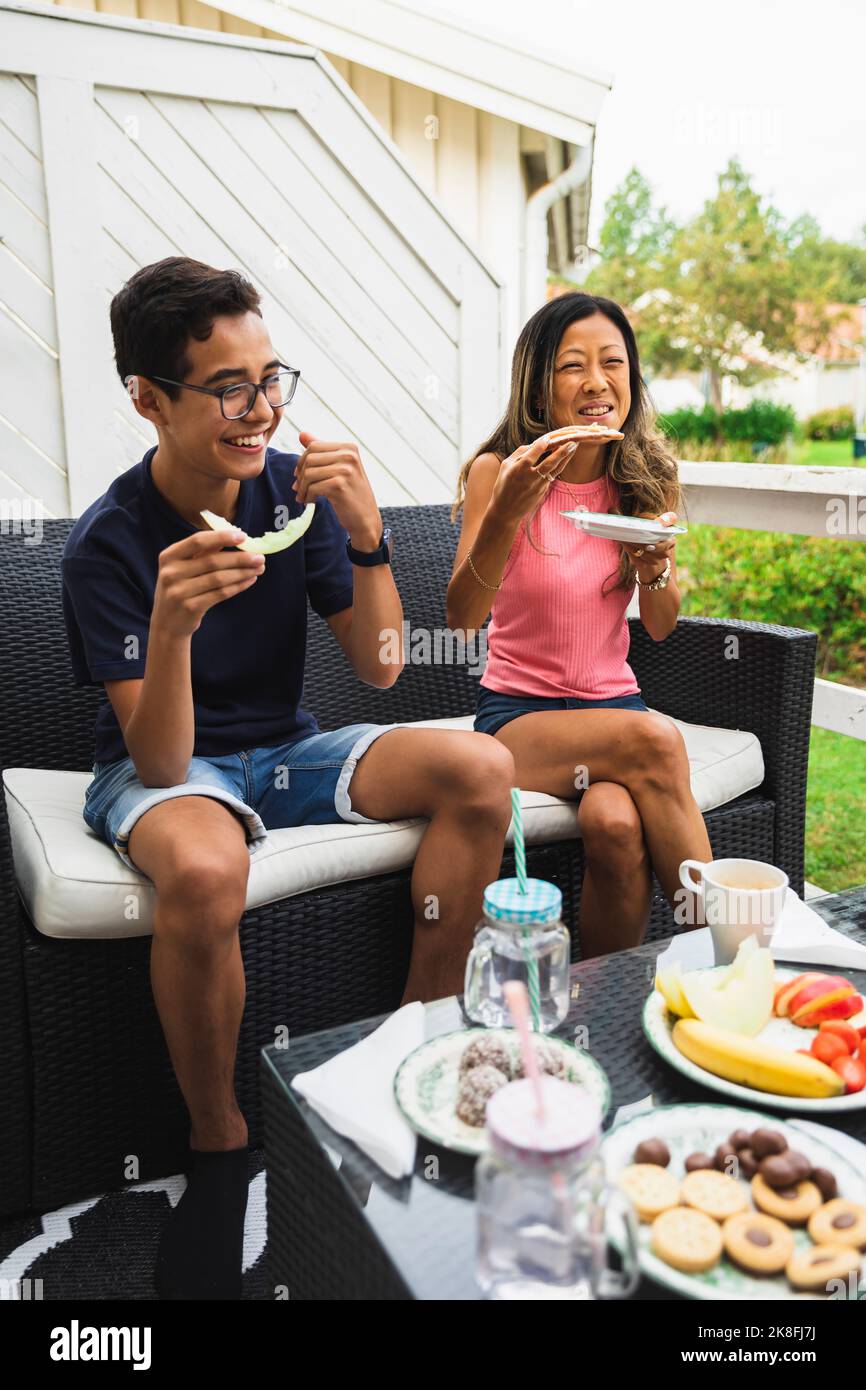 Happy woman enjoying snacks with son on couch at porch Stock Photo - Alamy