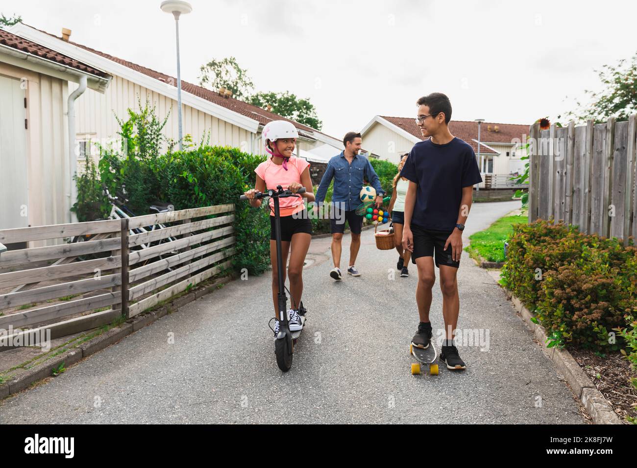 Brother with skateboard looking at sister riding electric scooter on ...