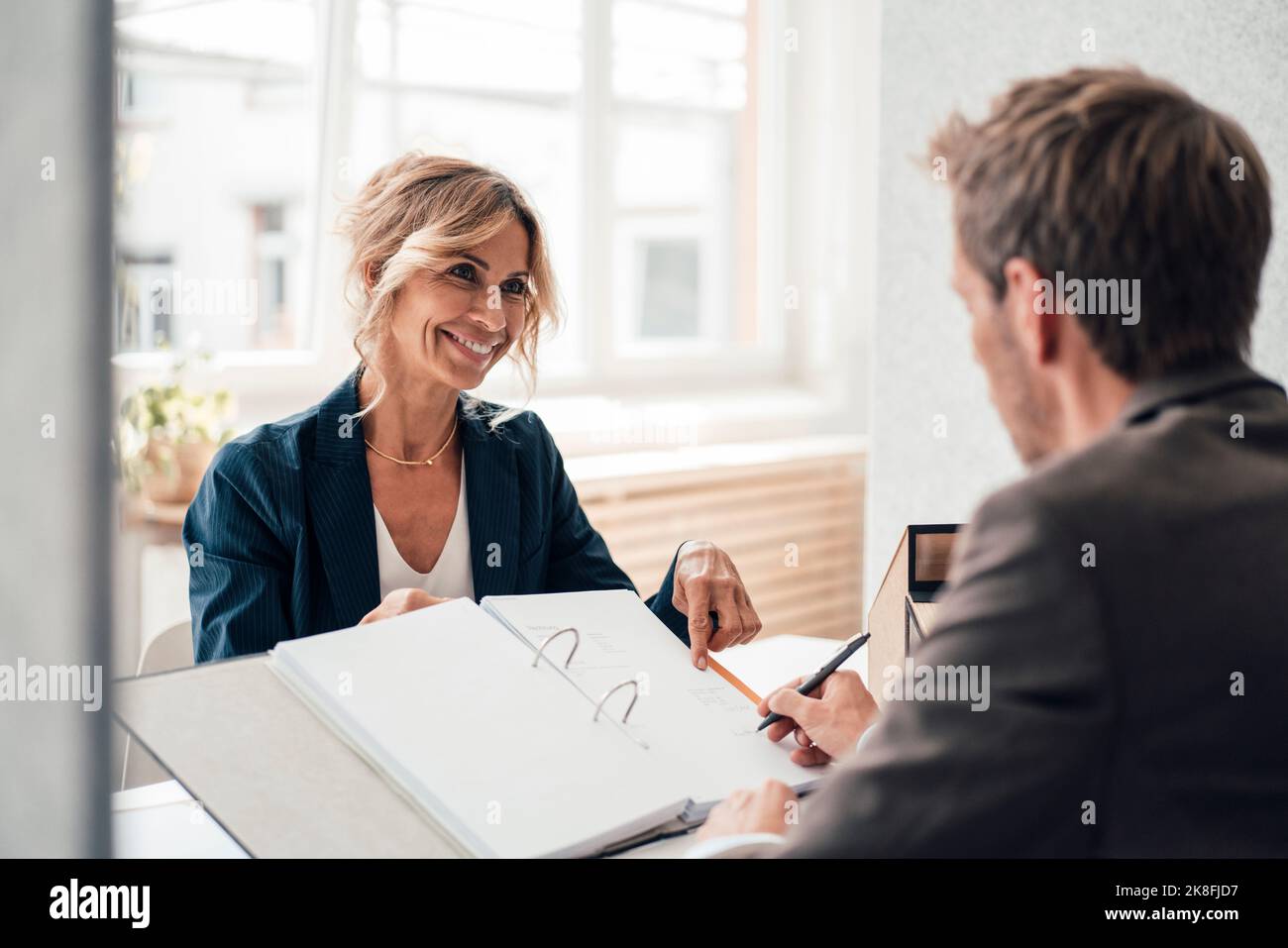 Smiling real estate agent assisting customer signing agreement at ...