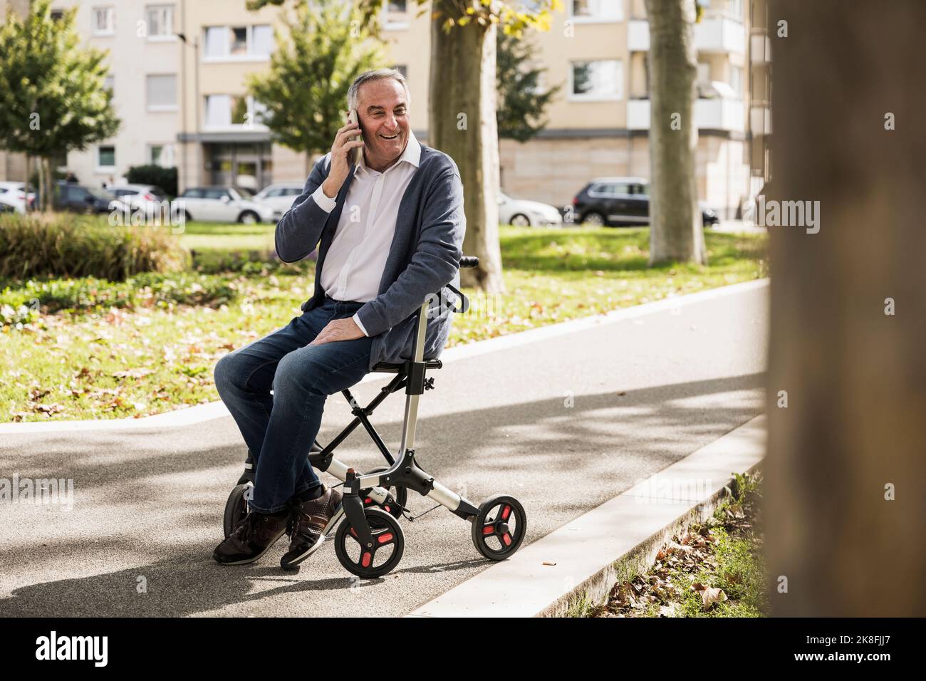 Happy senior man talking on mobile phone sitting on mobility walker ...