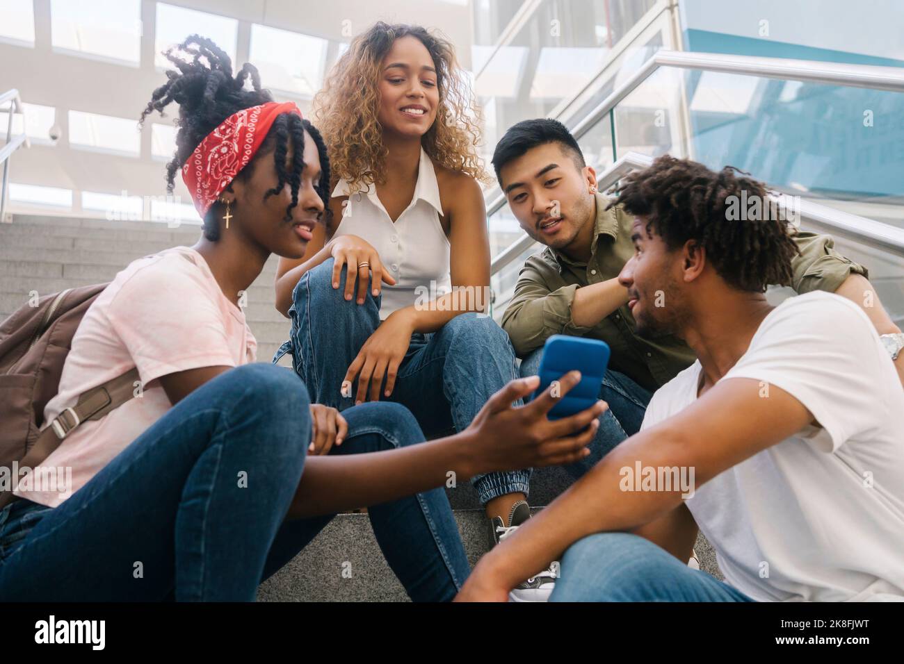Woman sharing mobile phone with multiracial friends on staircase Stock ...