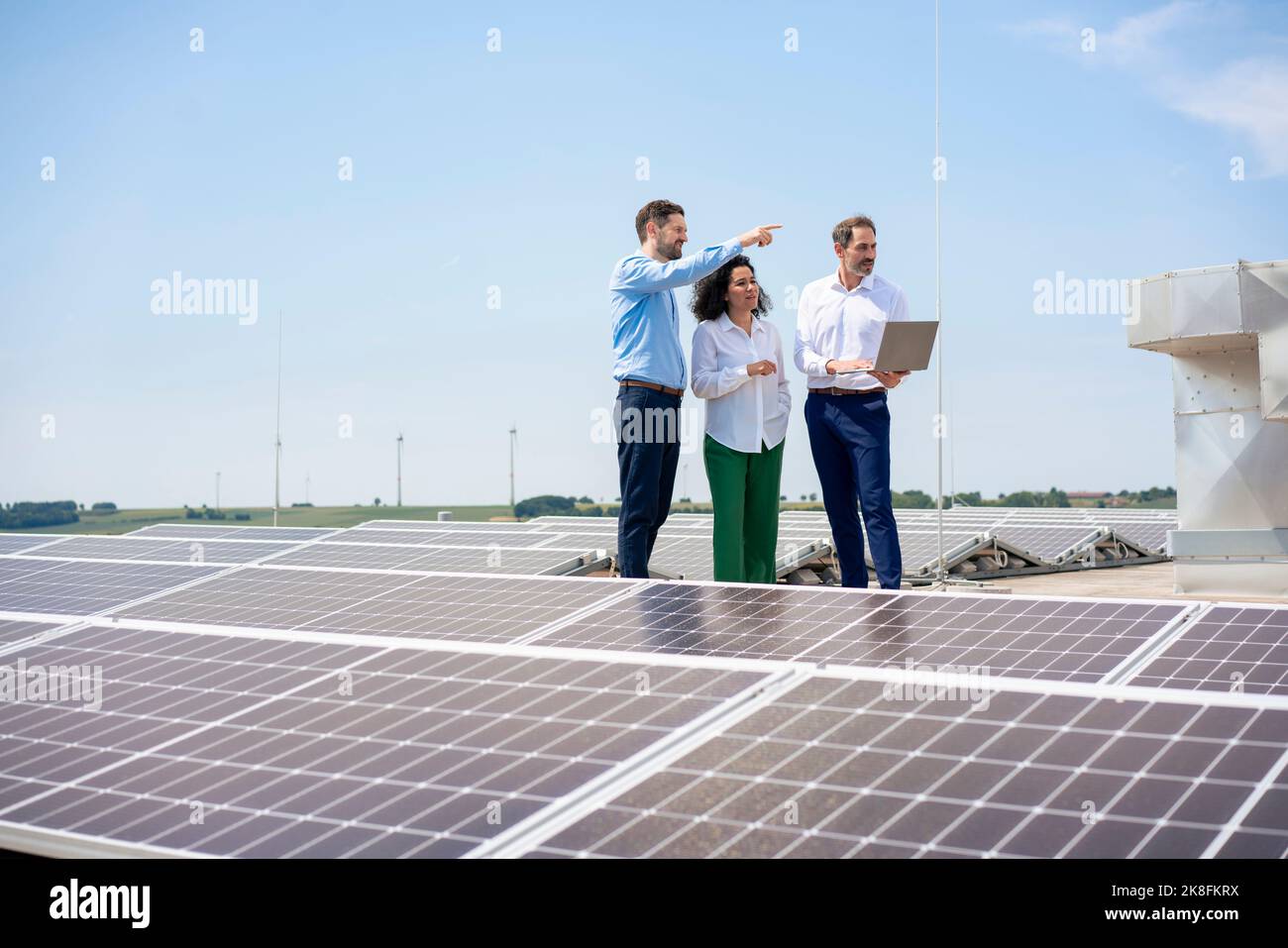 Businessman gesturing to colleagues discussing by solar panels on ...