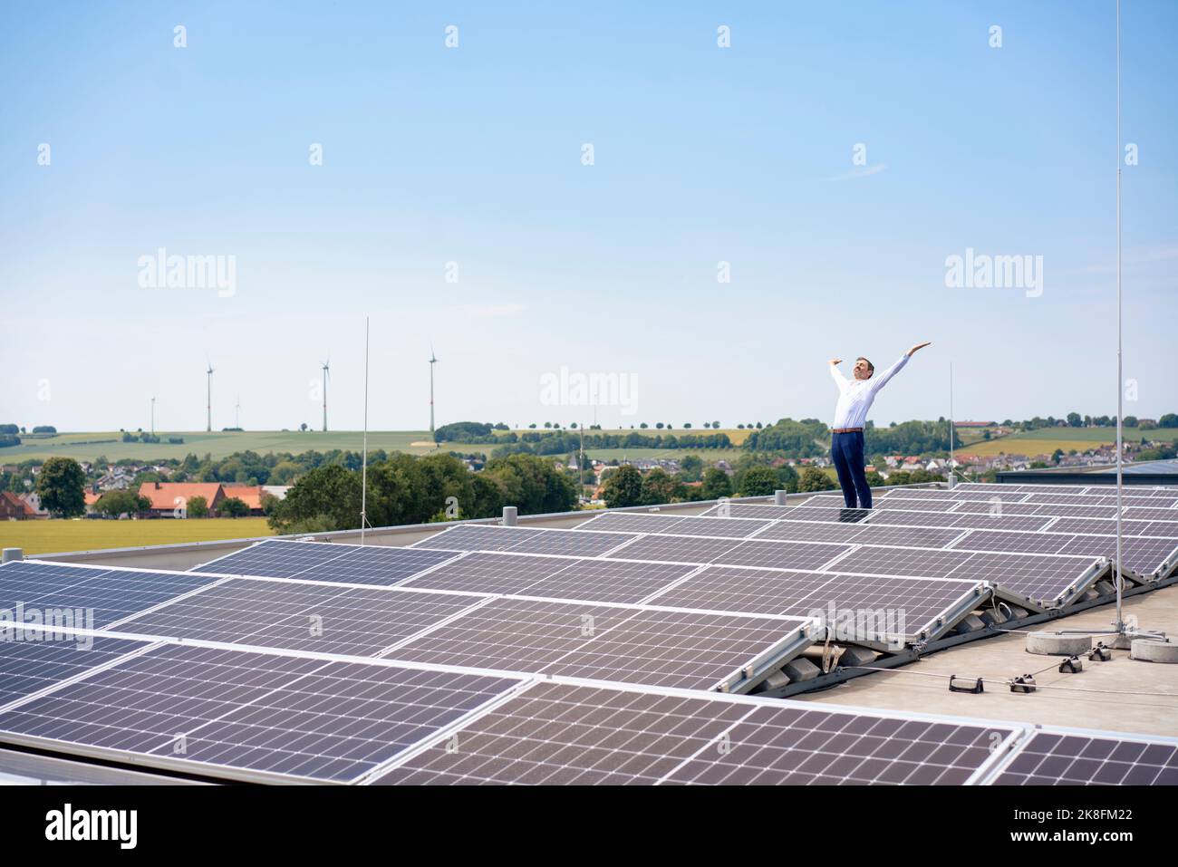 Mature businessman with arms raised amidst solar panels on rooftop ...