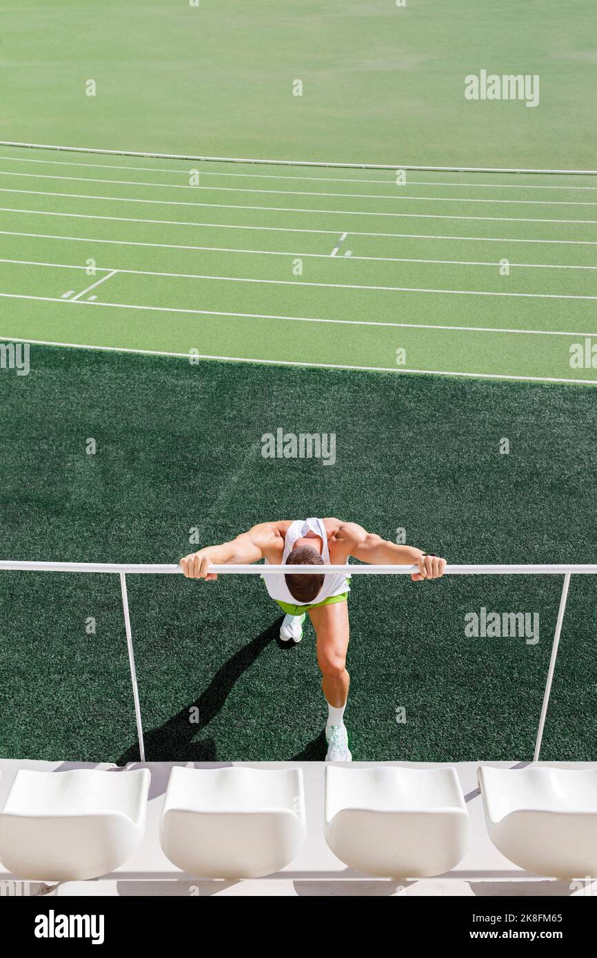 Athlete doing warm exercise by railing on sports field Stock Photo - Alamy