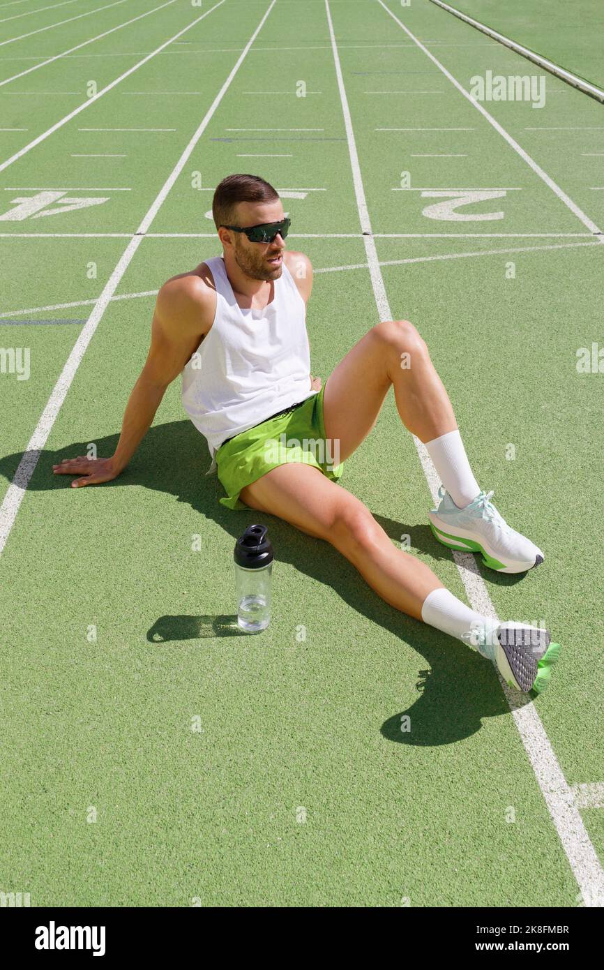 Tired athlete wearing sunglasses relaxing on sports track Stock Photo ...