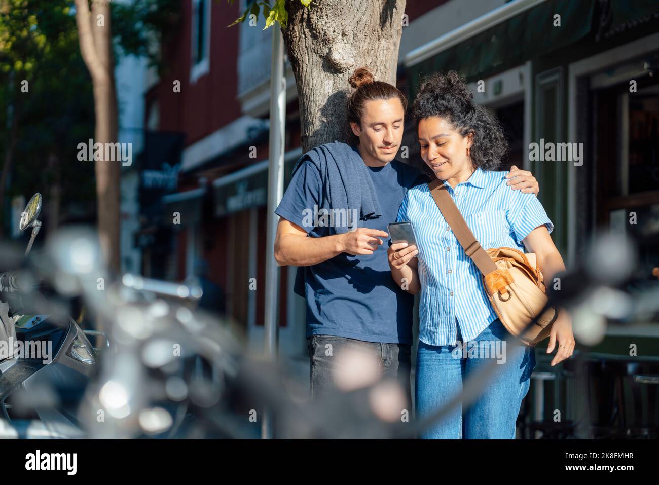 Woman sharing mobile phone with boyfriend by tree trunk Stock Photo - Alamy