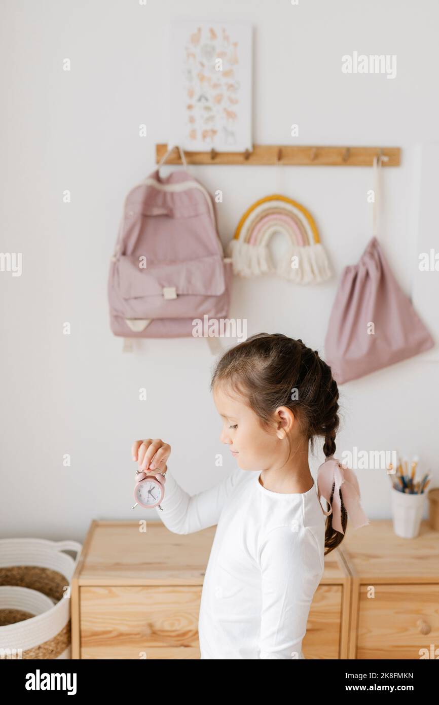 Girl standing at home looking at alarm clock Stock Photo - Alamy