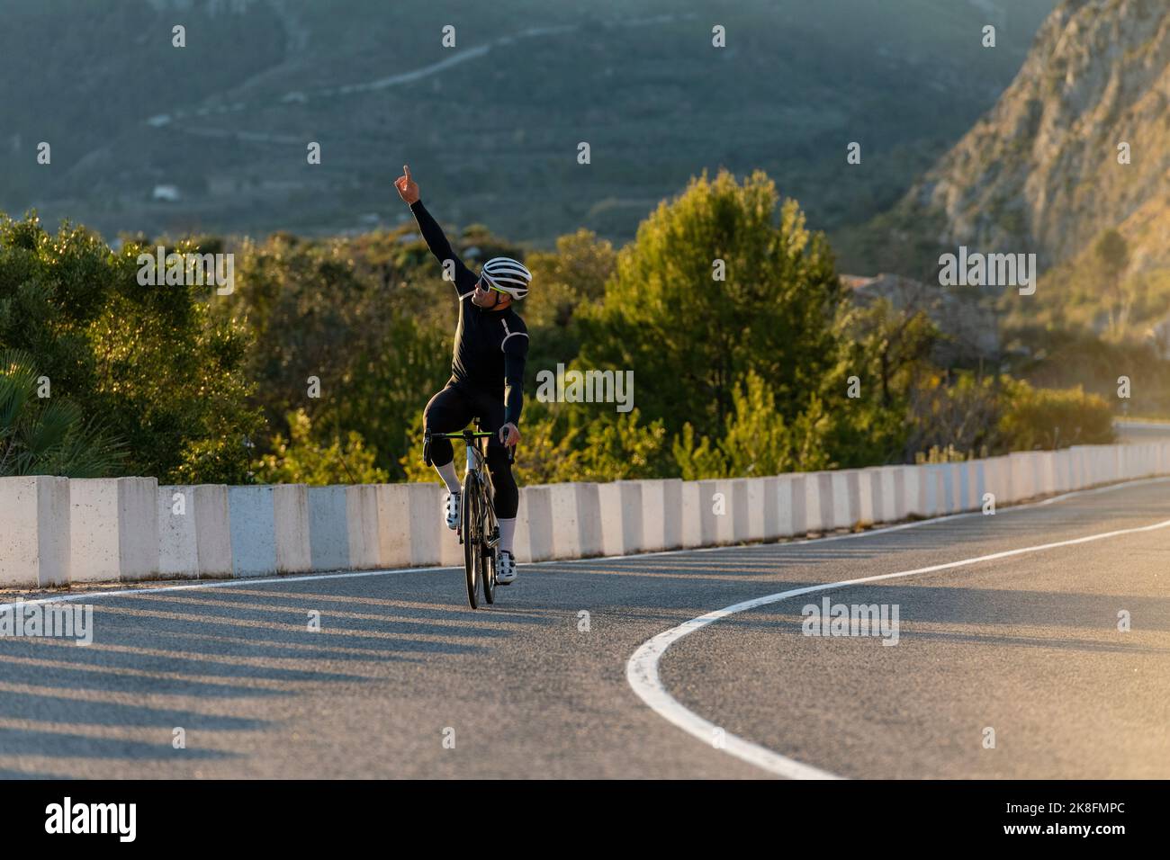 Cyclist with hand raised riding cycle on Costa Blanca mountain pass in ...