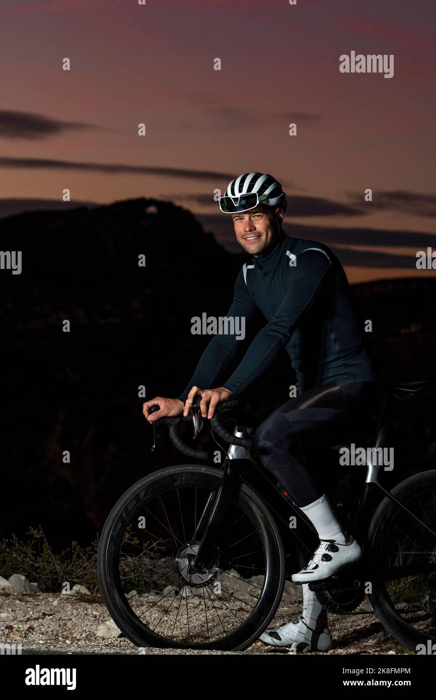 Smiling cyclist wearing helmet with bicycle at dusk Stock Photo - Alamy