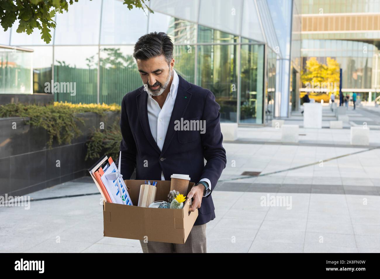 Sad businessman looking at office supplies in box standing near ...
