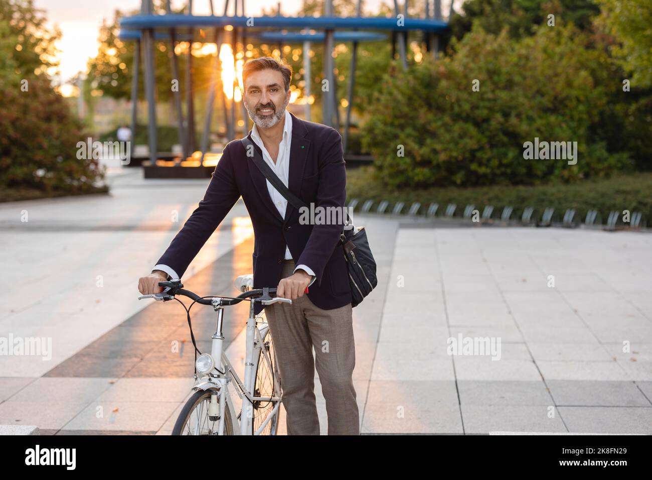 Smiling commuter wheeling with bicycle on footpath Stock Photo - Alamy