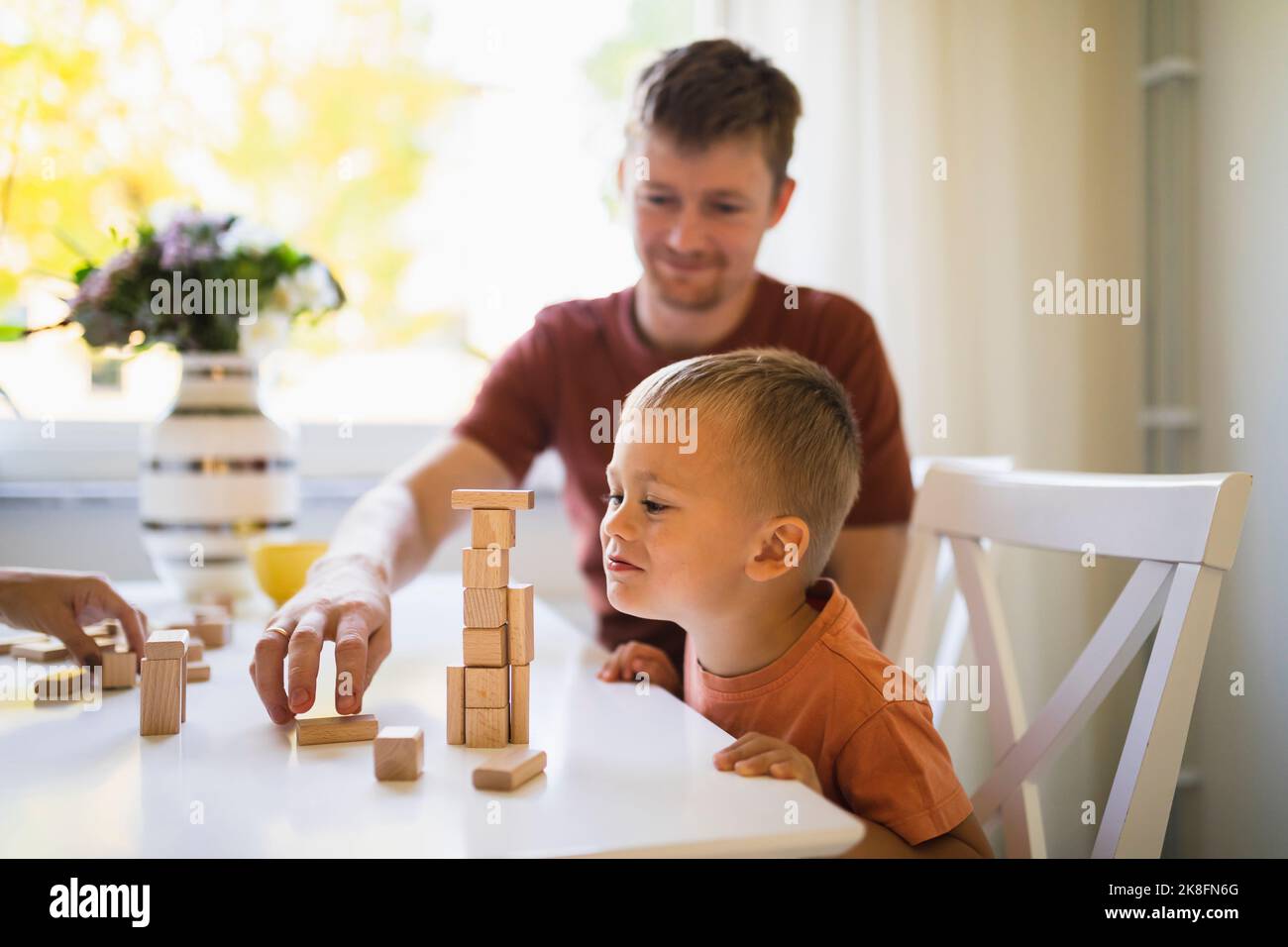 Cute boy looking at father stacking toy blocks on dining table Stock ...