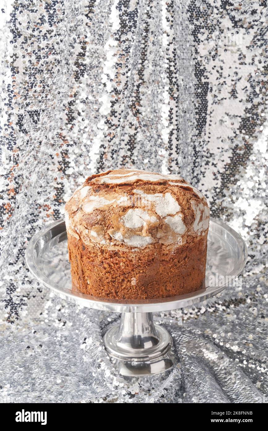 Freshly baked panettone cake on cakestand against shiny silver sequins ...