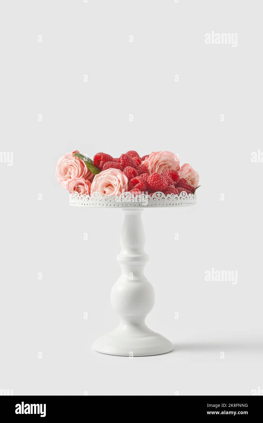 Raspberries with roses on pedestal cakestand against white background ...