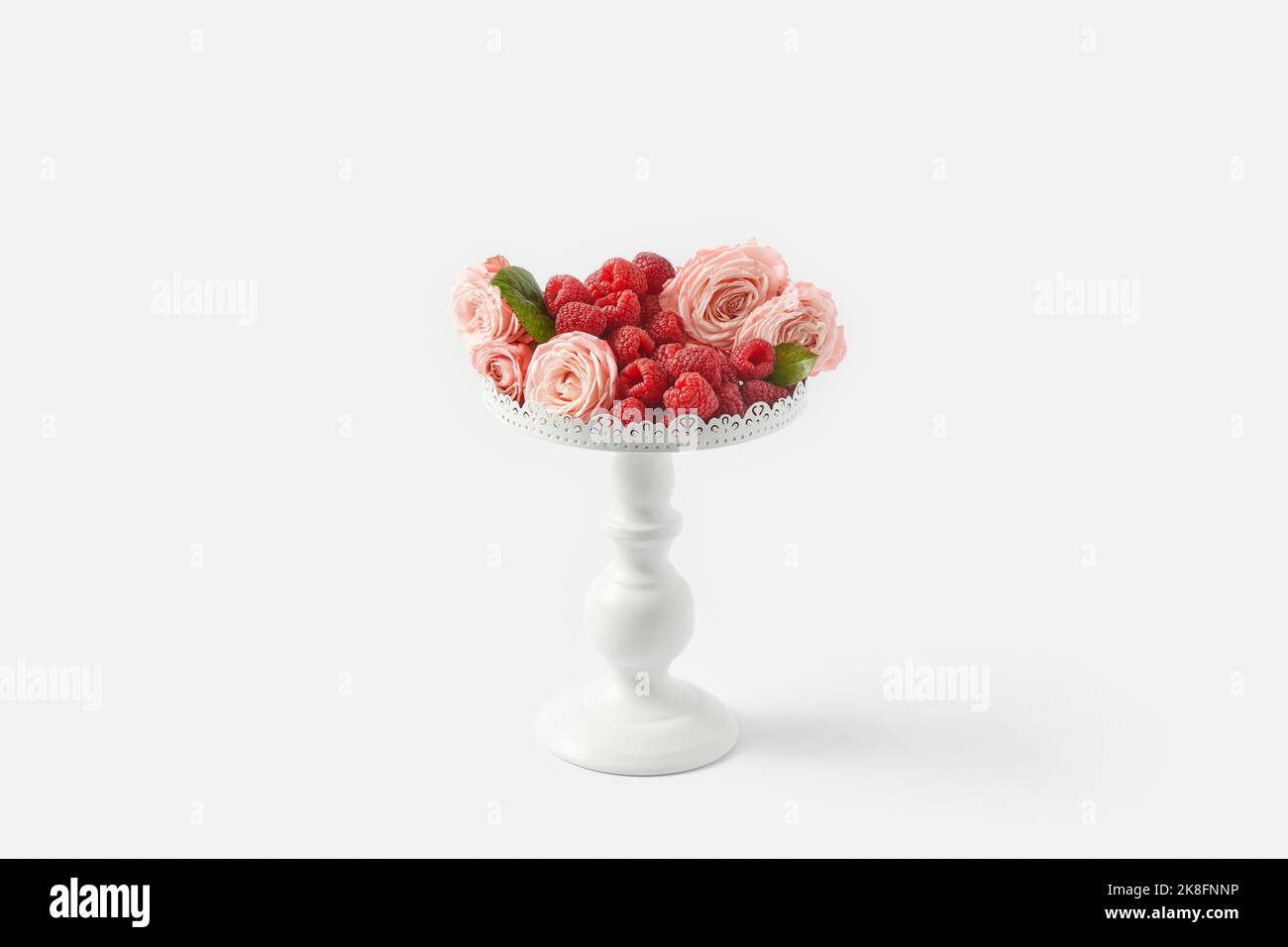 Raspberries with pink roses on pedestal cakestand against white ...