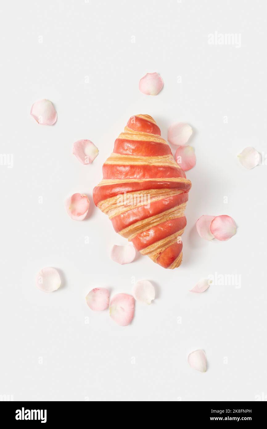 Freshly baked croissant amidst rose petals against white background ...