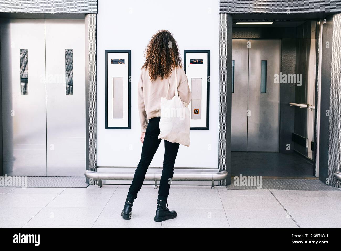 Woman with curly hair standing in front of elevator Stock Photo - Alamy