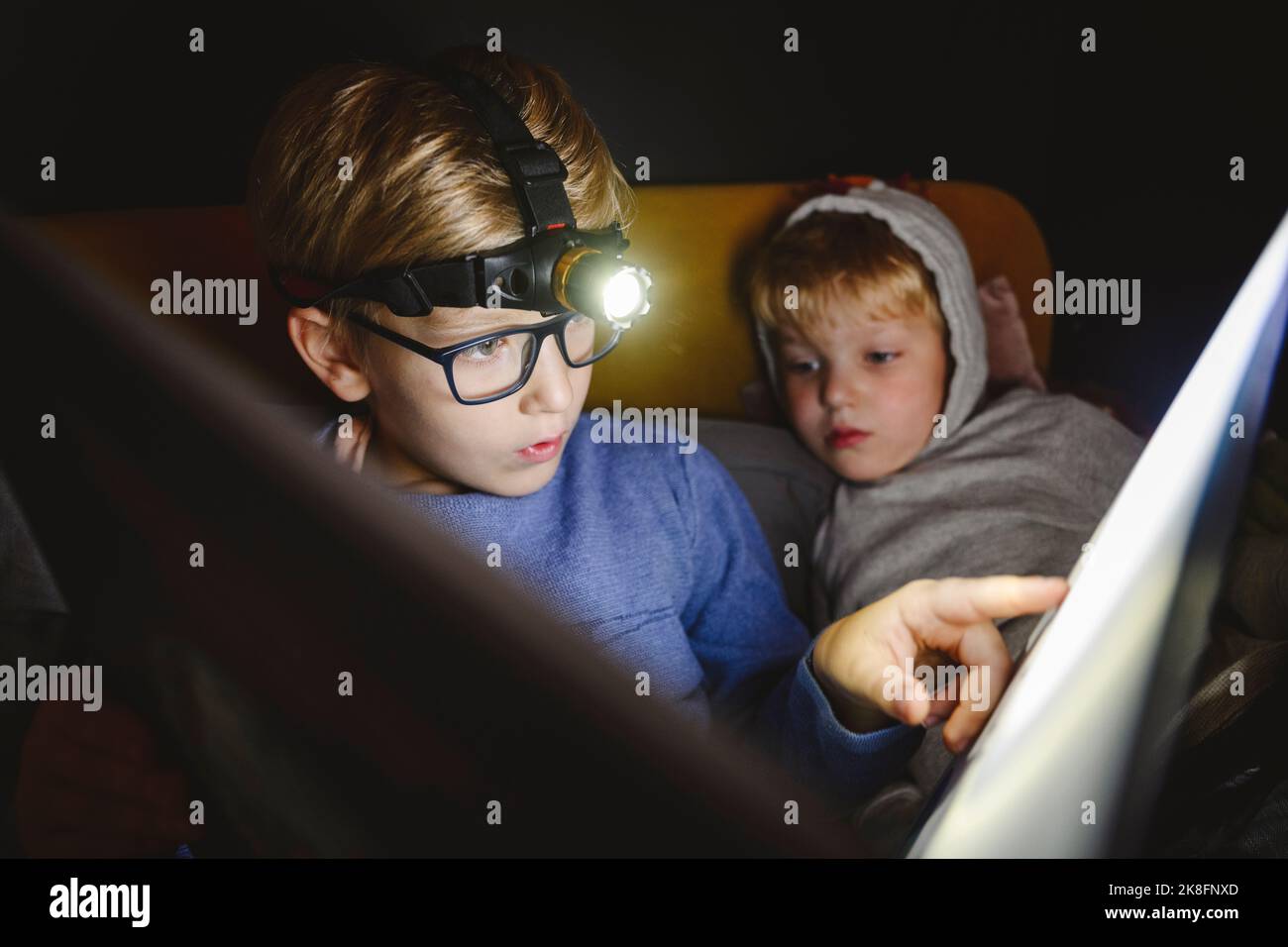 Boy wearing headlight reading book with brother at home Stock Photo - Alamy