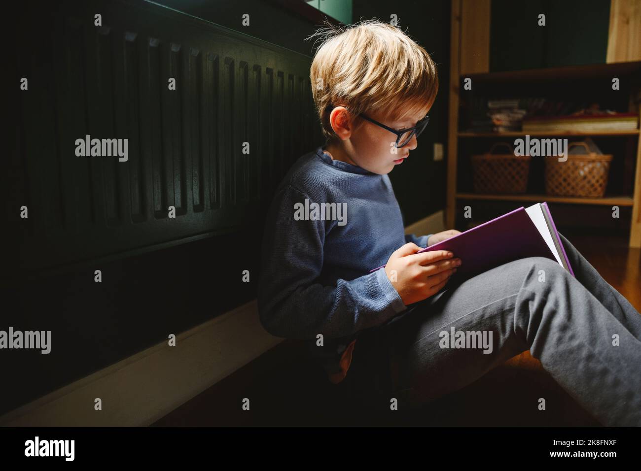 Boy wearing eyeglasses reading book sitting on floor at home Stock ...