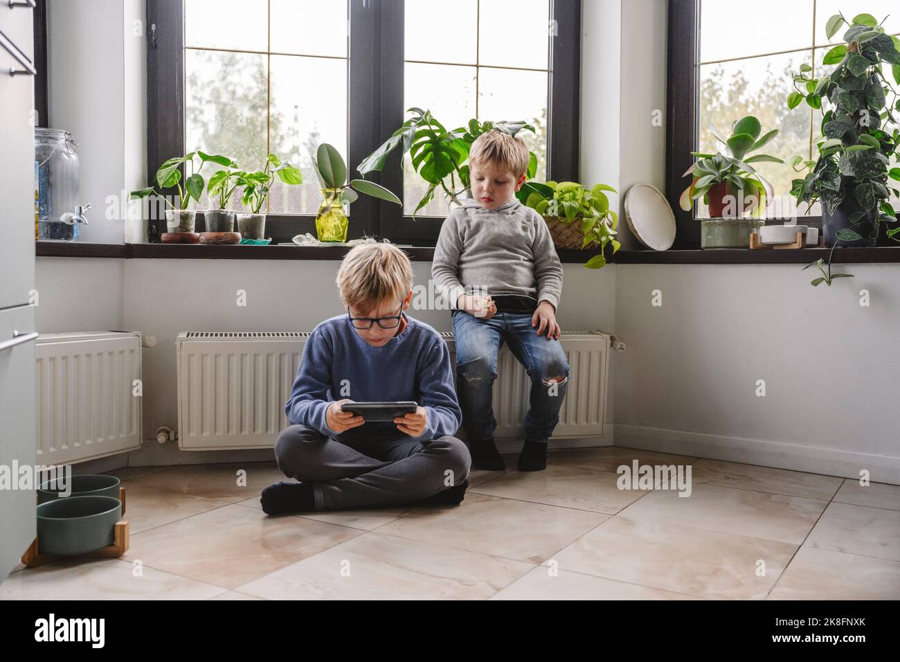 Boy sitting on radiator with brother using smart phone at home Stock ...