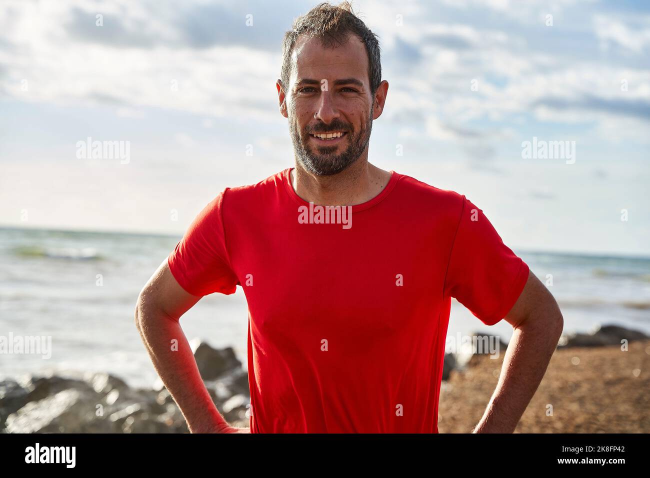Smiling man with hands on hips at beach Stock Photo - Alamy