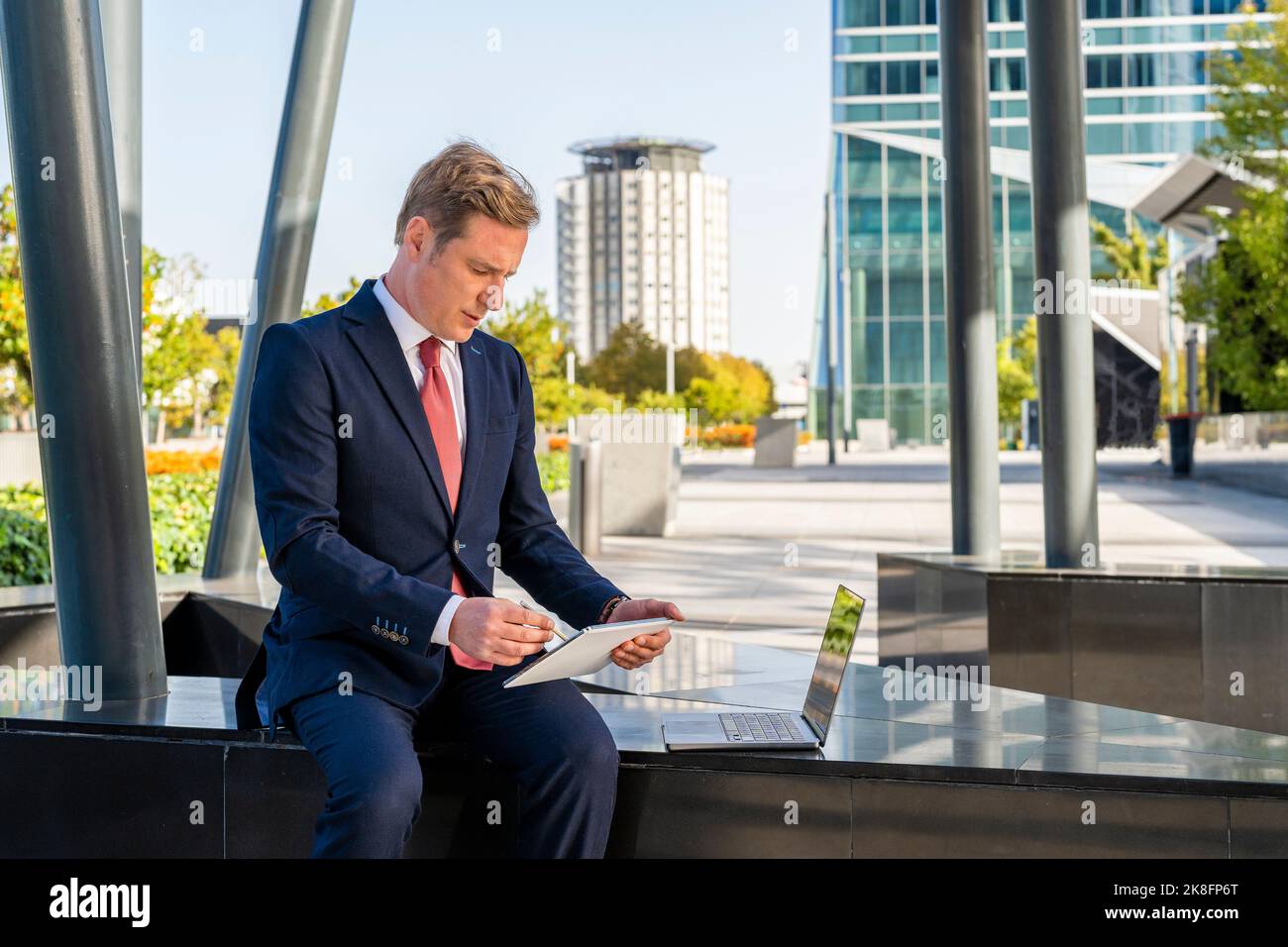 Businessman using tablet PC sitting with laptop in office park Stock ...