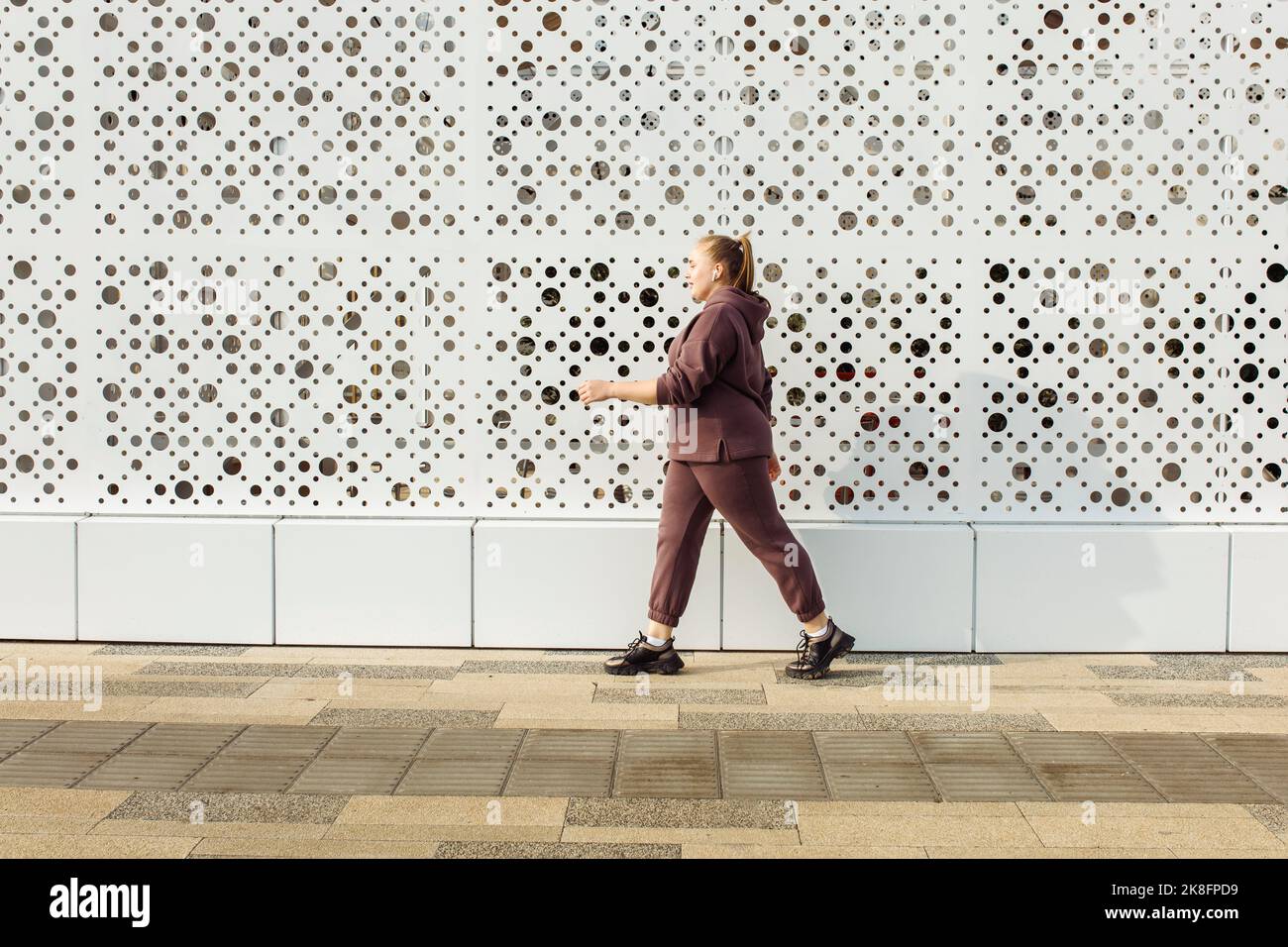 Overweight woman in hooded shirt walking along wall Stock Photo - Alamy