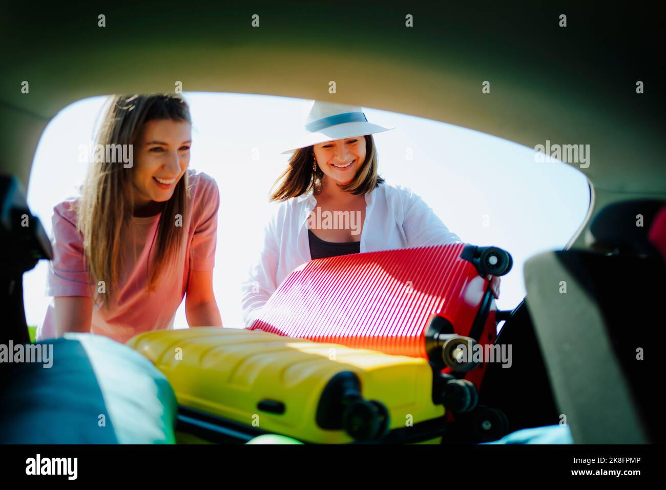 Happy friends loading suitcase in car trunk Stock Photo - Alamy