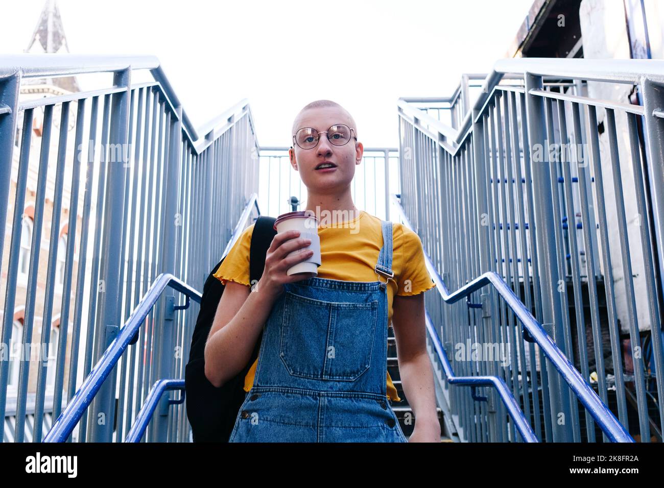 Thoughtful transgender person with disposable coffee cup on staircase ...