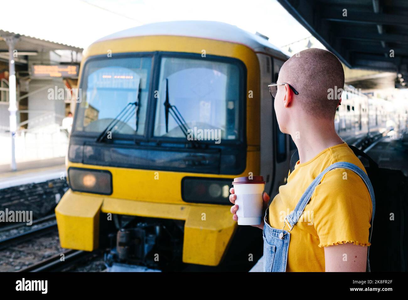 Transgender person with disposable coffee cup looking at train arriving ...