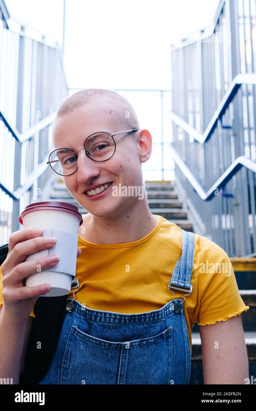 Smiling non-binary person with disposable coffee cup wearing eyeglasses ...