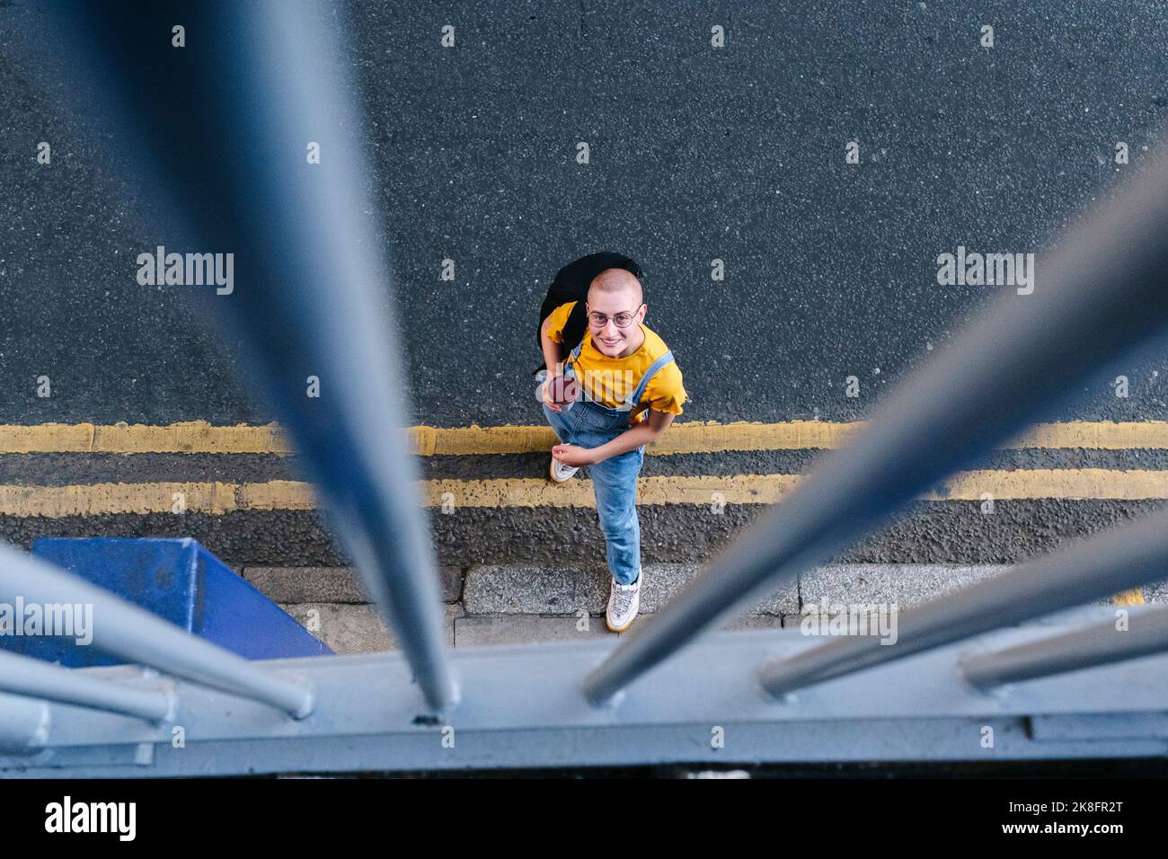 Smiling non-binary person with backpack seen through railings on street ...