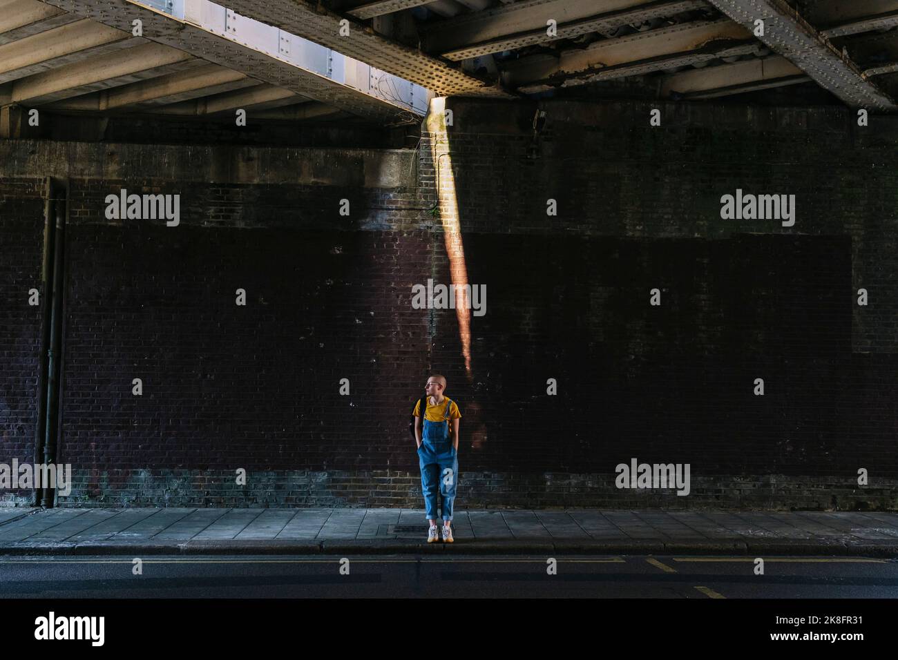 Young androgynous person waiting on sidewalk below bridge Stock Photo ...