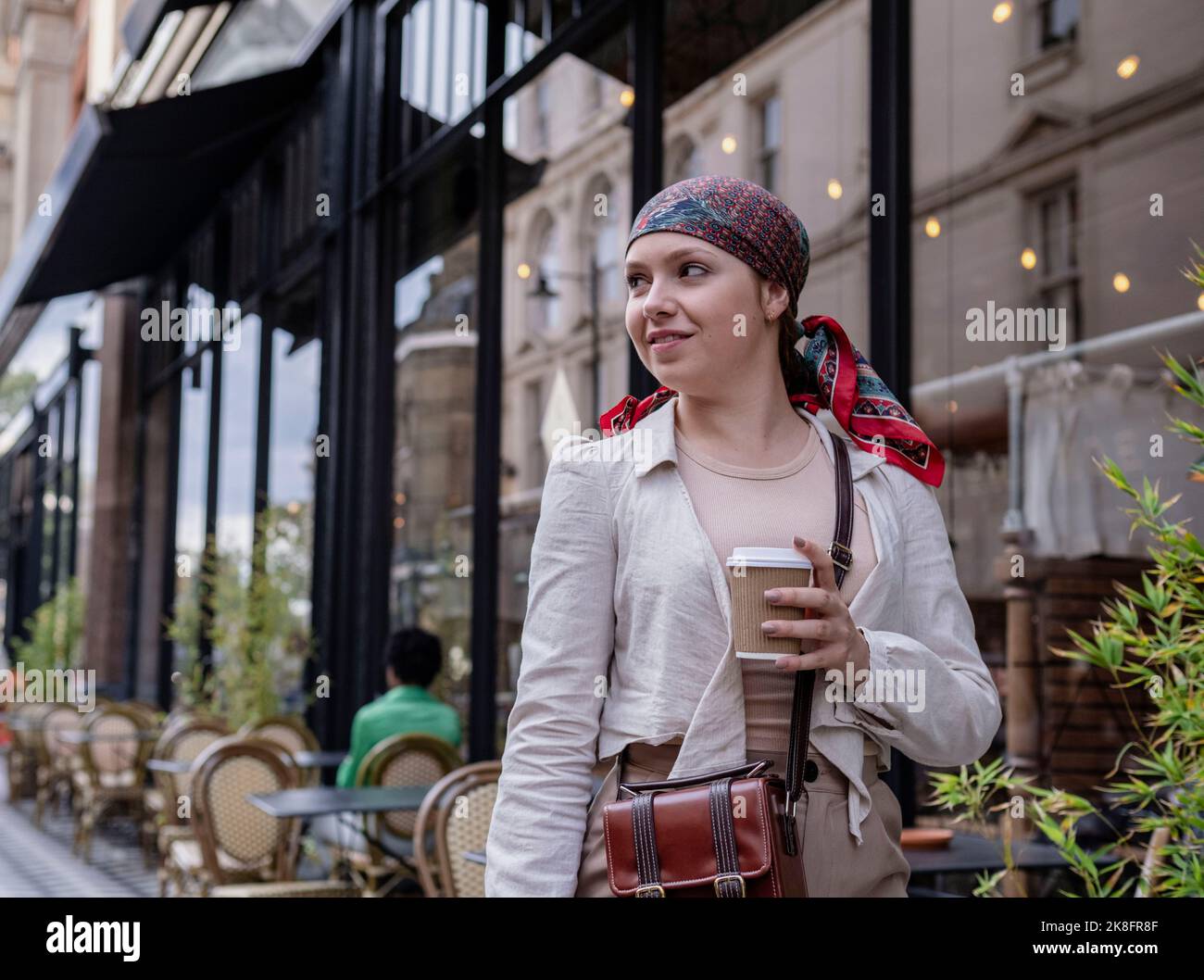 Young woman wearing bandana holding disposable cup at sidewalk cafe ...