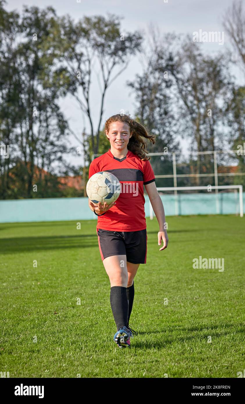 Happy girl walking with soccer ball on field Stock Photo - Alamy
