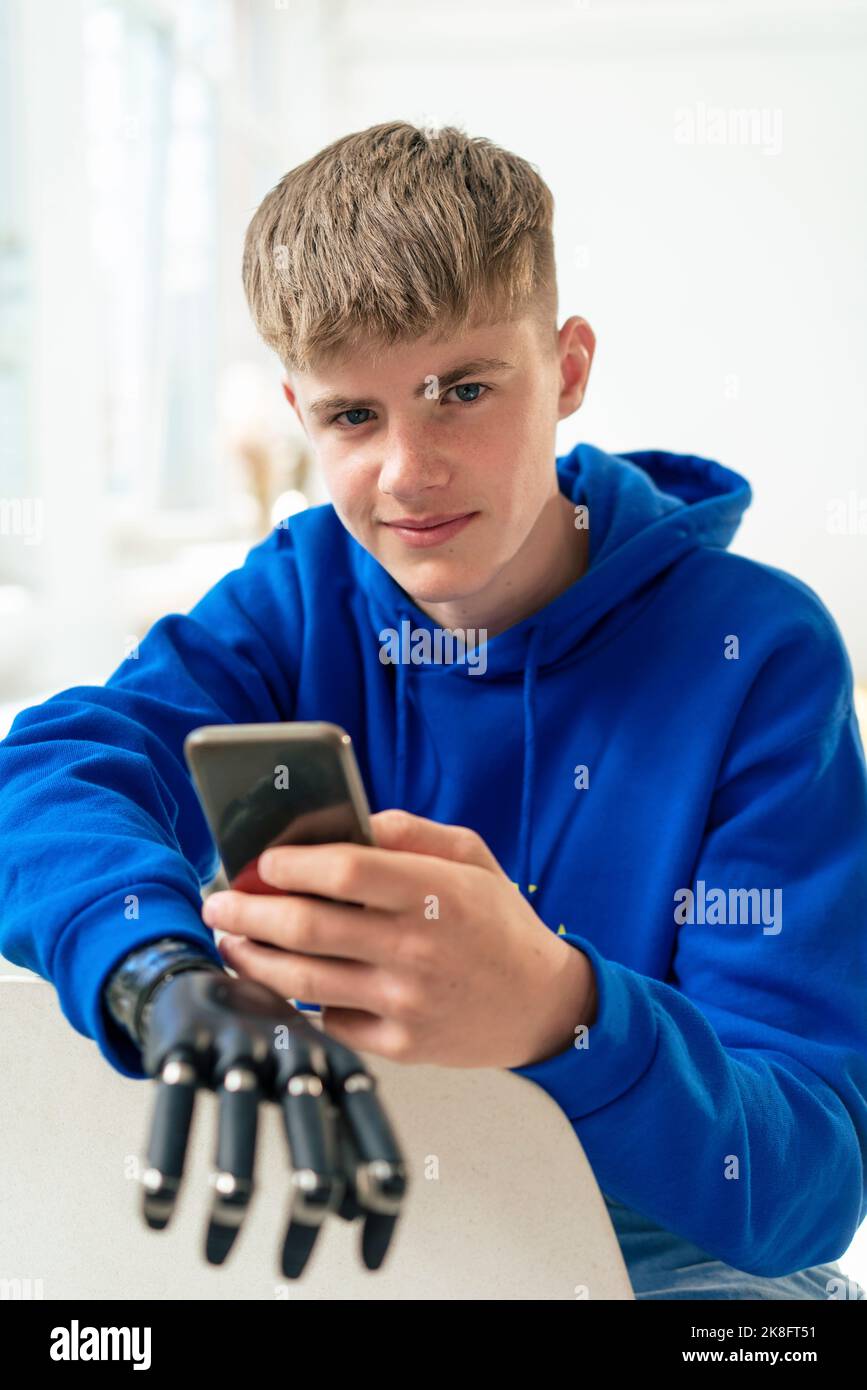 Boy with prosthetic arm using smart phone sitting on chair Stock Photo ...