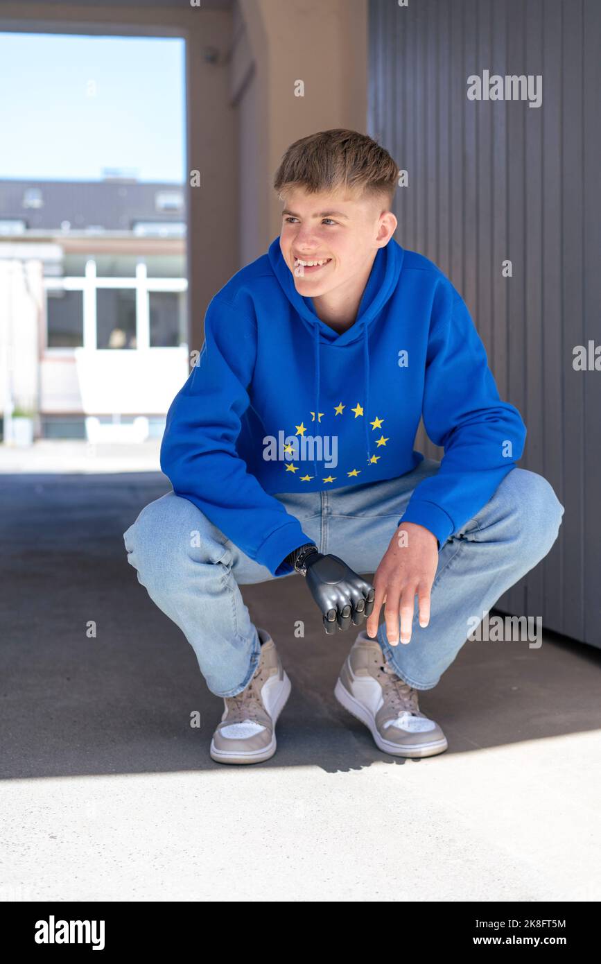 Smiling boy with prosthetic arm crouching under shadow Stock Photo - Alamy