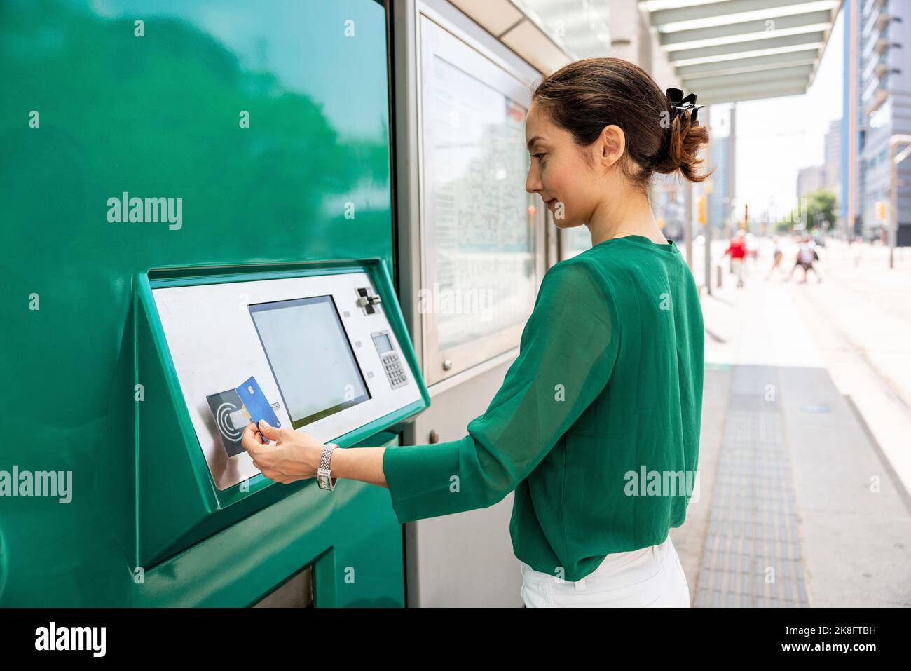 Smiling woman operating ticket machine with credit card at tram stop ...