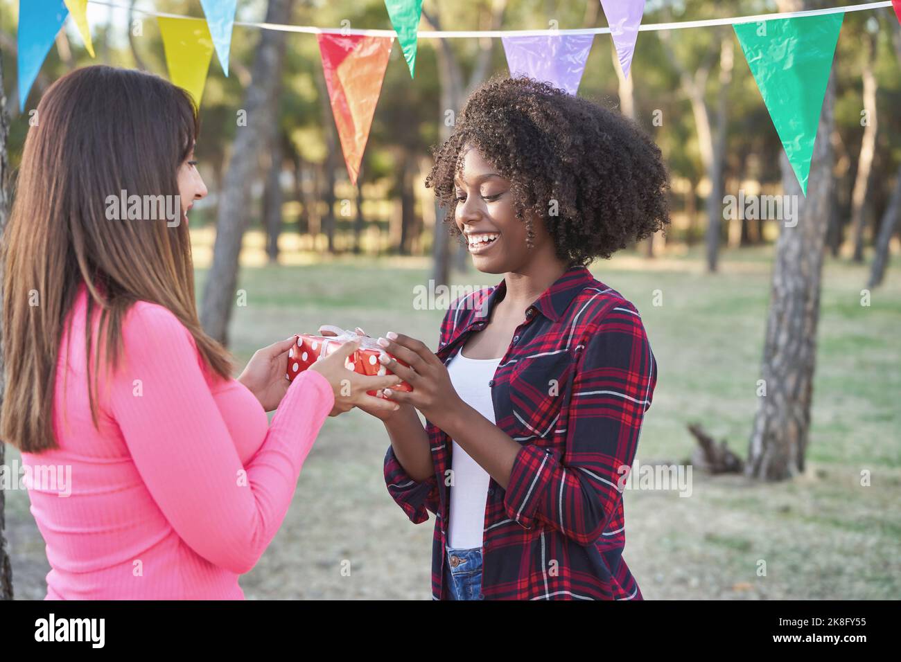 Woman giving a gift to her friend while having a party outdoors in a ...