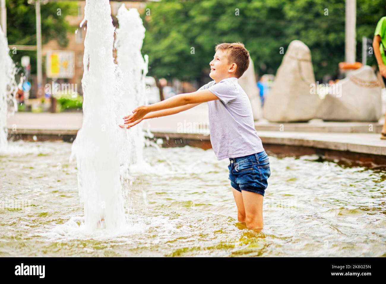 A boy having fun in water fountains. Child playing with a city fountain ...
