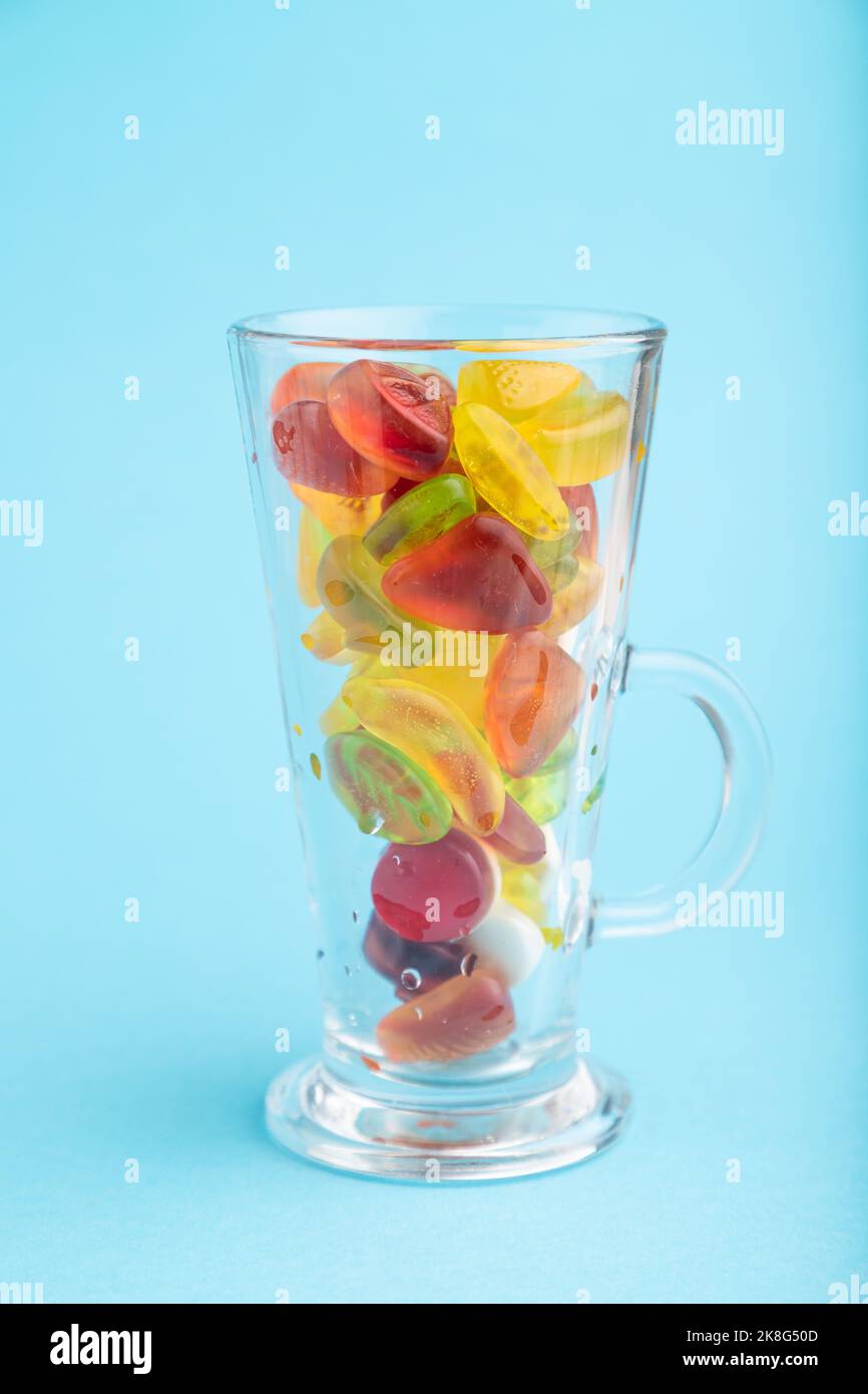 Various fruit jelly candies in drinking glass on blue pastel background ...