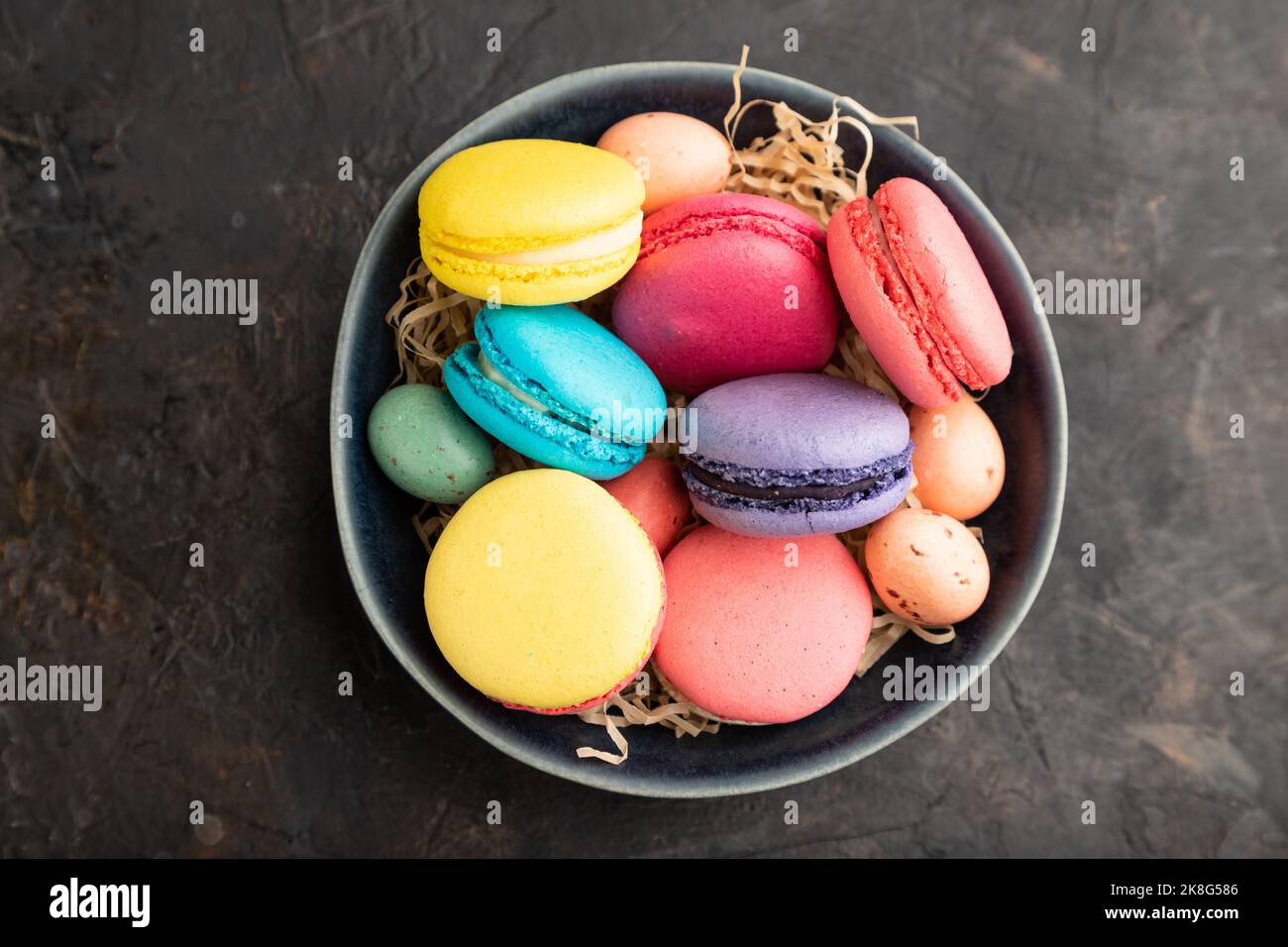 Multicolored macaroons and chocolate eggs in ceramic bowl on black ...
