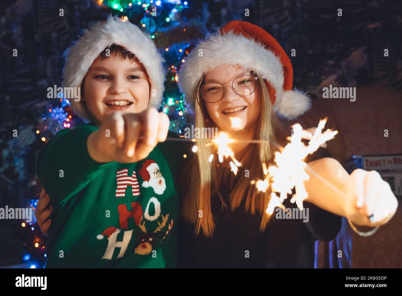 Happy teen girl wearing Santa hat, cute boy holding burning sparkler ...