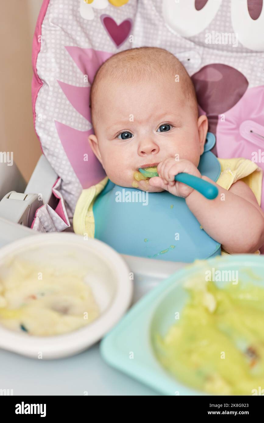 cute baby girl eating with spoon in kitchen Stock Photo - Alamy
