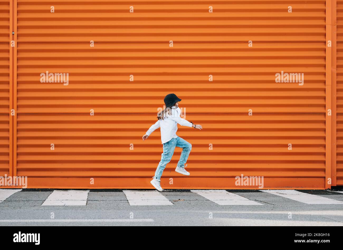 Little fashion-dressed girl funny jumping crossing a pedestrian zebra ...