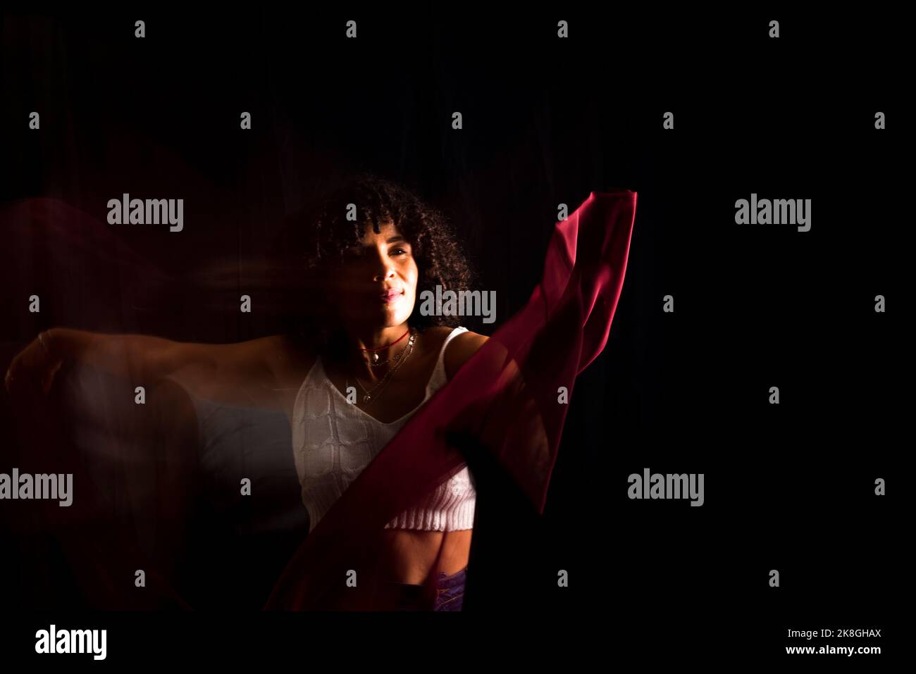 Woman moving a red cloth over her head against a black background ...