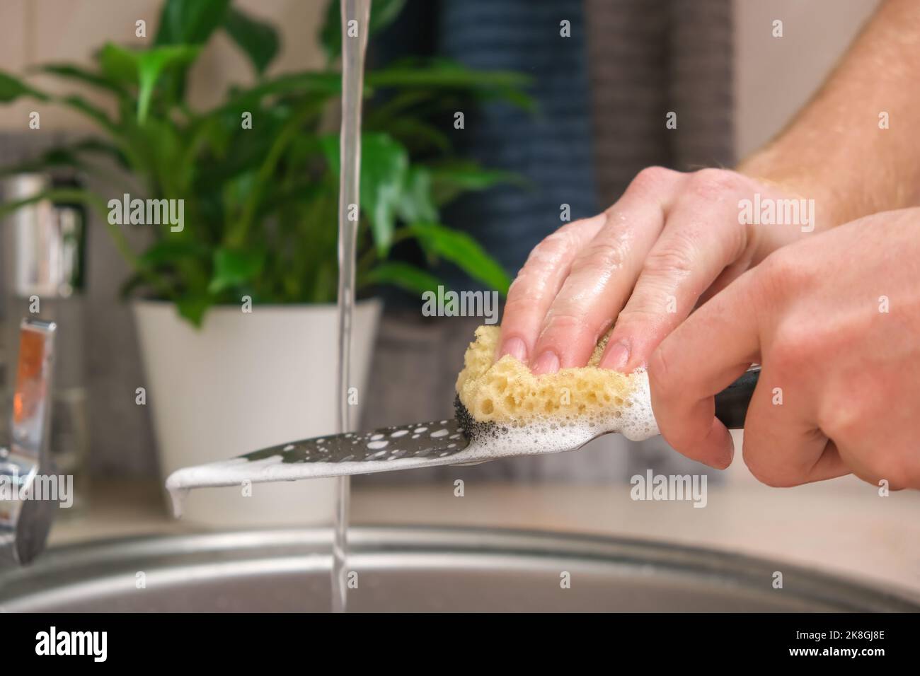 A man washes a sharp steel dirty kitchen knife with a sponge with ...