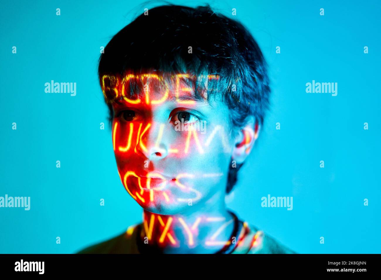 Portrait of unemotional boy with big sad eyes in room with neon light ...