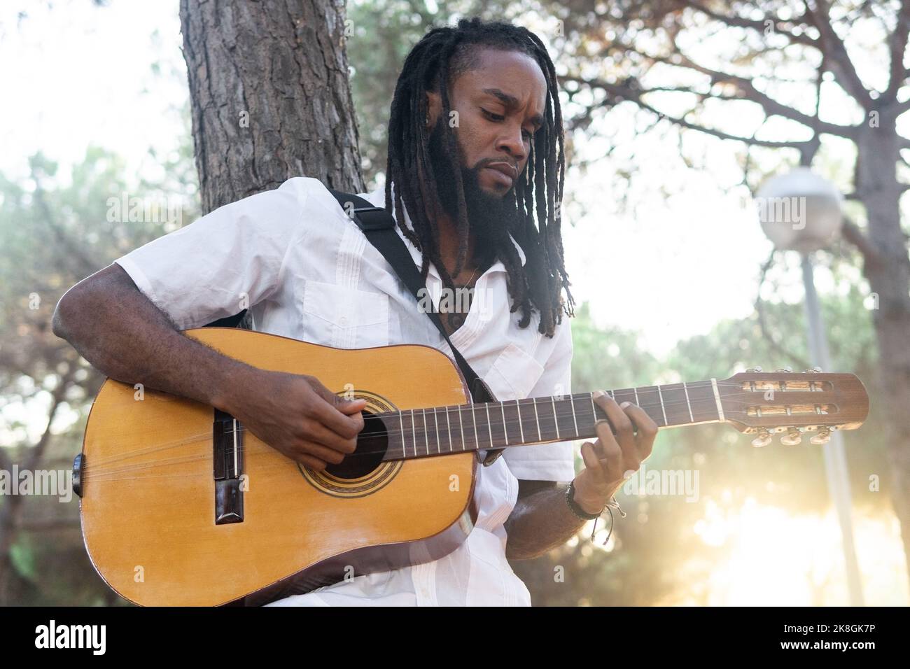 African American musician with dreadlocks playing acoustic guitar while ...